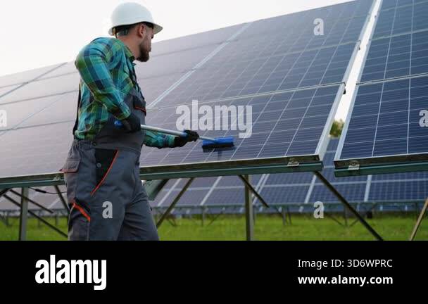 Male engineer in a helmet and uniform cleaning solar panels with a ...