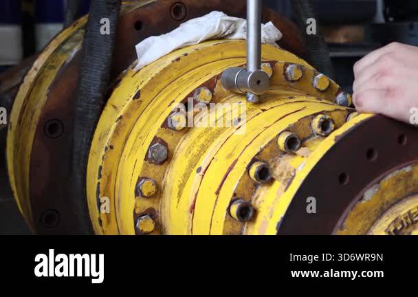 A mechanic's hand operates a large T-handle on the heavily bolted, worn ...