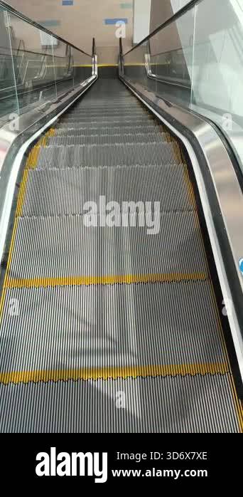 A clean, modern escalator with glass and chrome railings. The metal ...