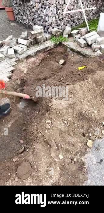 A worker throws earth with a shovel into a deep trench for building a ...
