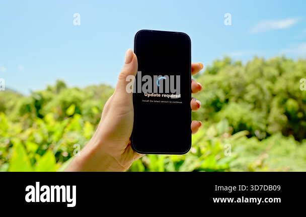 Smartphone in Hand Displaying Update Required Screen Against Sunny Sky ...