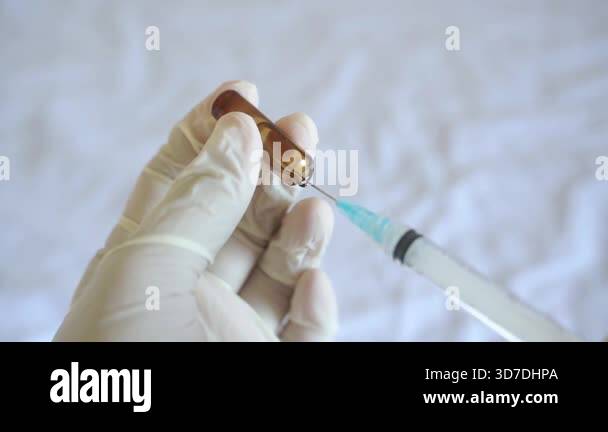 Gloved hands drawing liquid medication from an open glass ampoule using ...