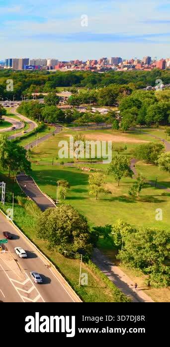 Green park with walking paths and trees bordered by roads and mid-rise ...