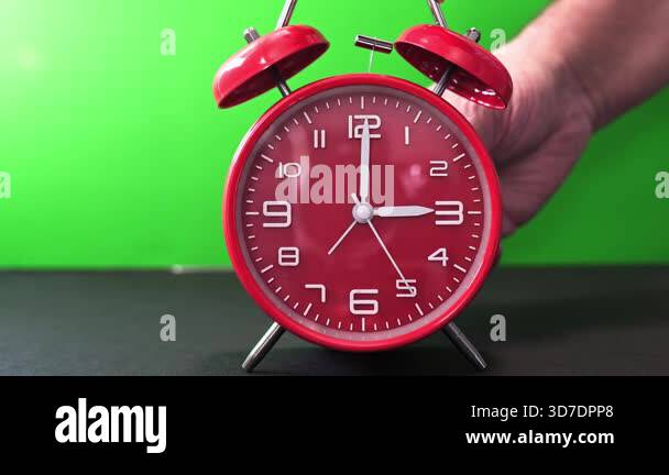 person gently sets a red alarm clock while its hands move from 3AM to 2AM in Daylight saving ...