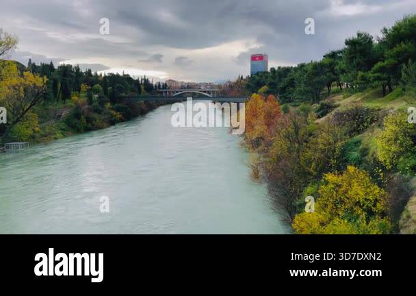river flowing between autumn trees under cloudy sky, pale teal water ...