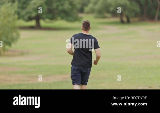 Rear view of a man running alone across a green grassy field during his ...