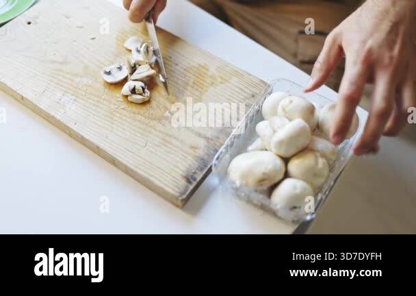 Man preparing a meal by slicing fresh white champignon mushrooms on a ...
