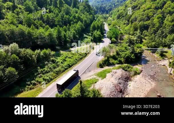 Trucks driving through green mountain pass. Freight vehicles move along ...