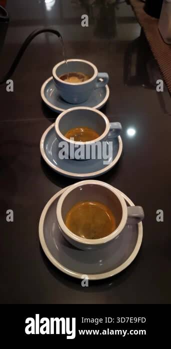 Three blue coffee cups on a dark reflective table are being filled with ...