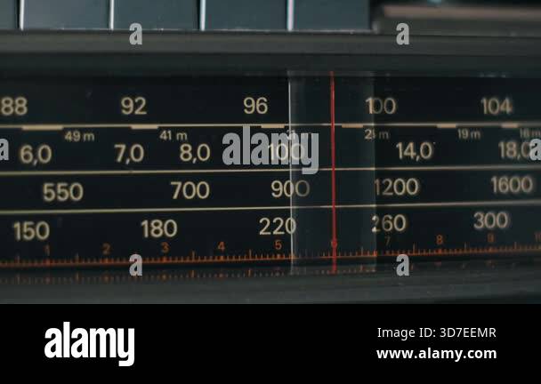 Macro shot of a vintage radio tuner dial. A red needle indicator moves ...
