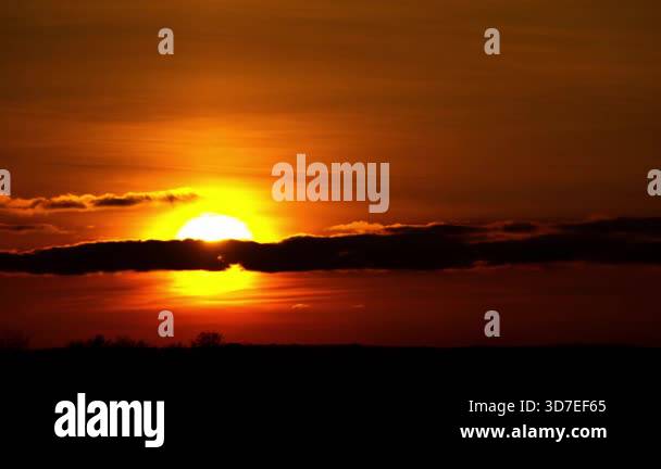 Timelapse of vibrant orange sun setting behind dark clouds at golden ...