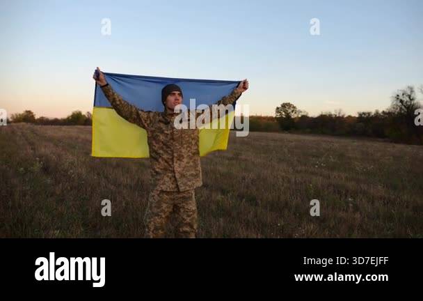 Young male military in uniform standing with raised flag Ukraine above ...