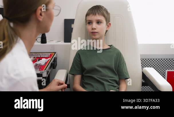 Cute boy sits in examination chair and talks with optometrist during ...
