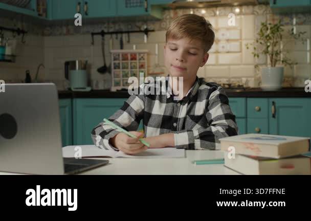 Young boy attending an online class on a laptop while writing notes in ...