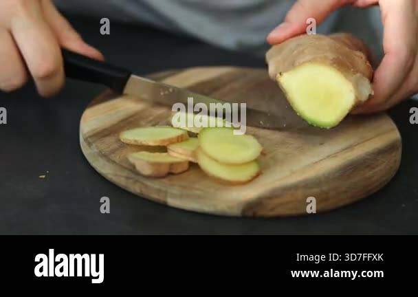 Close up of female hands cutting fresh ginger with a knife on wooden ...