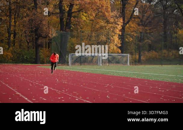 Man sprinting on red athletic track in autumn park. Front view of ...