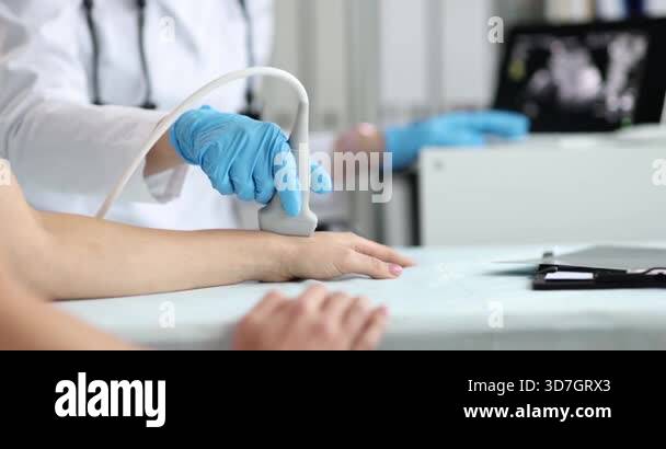 Patient arm rests on table while ultrasound probe touches wrist for ...
