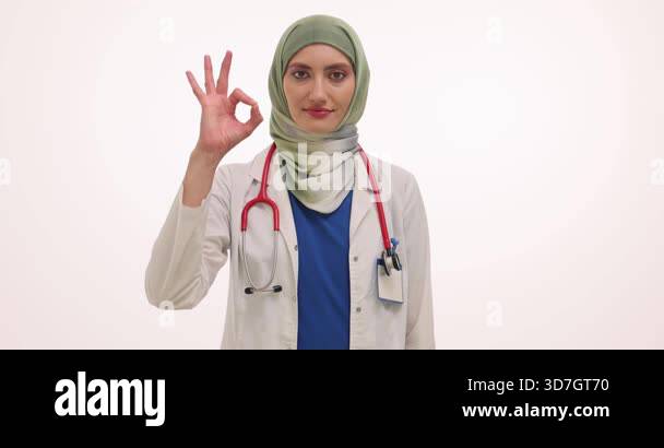 Muslim woman doctor raises OK sign smiling calmly. Medical expert wears ...