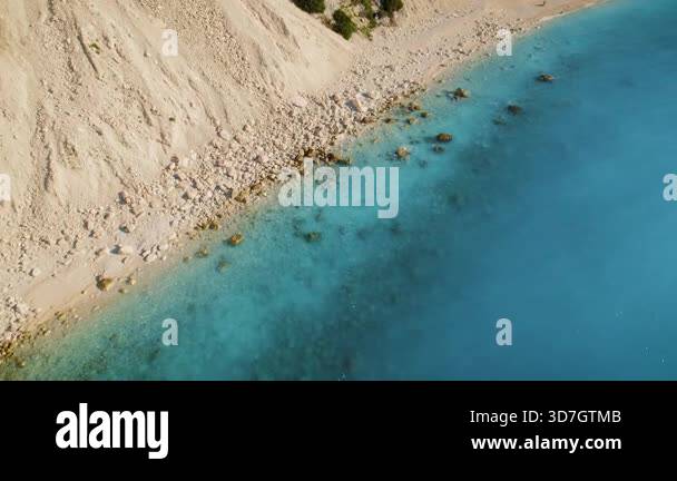 Rocky shoreline and clear shallow water along a Greek beach in sunny ...