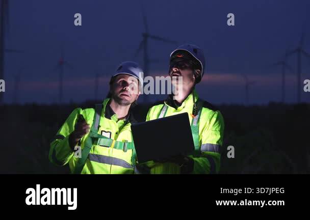 Engineers wearing safety helmets and jackets inspecting a wind turbine ...