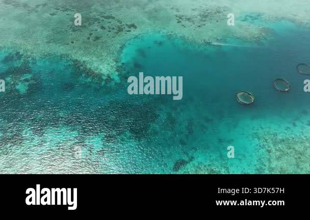 Coastal reef with turquoise water and round fish cages floating near ...