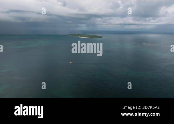 View of a green island across the wide sea under cloudy and rainy sky ...