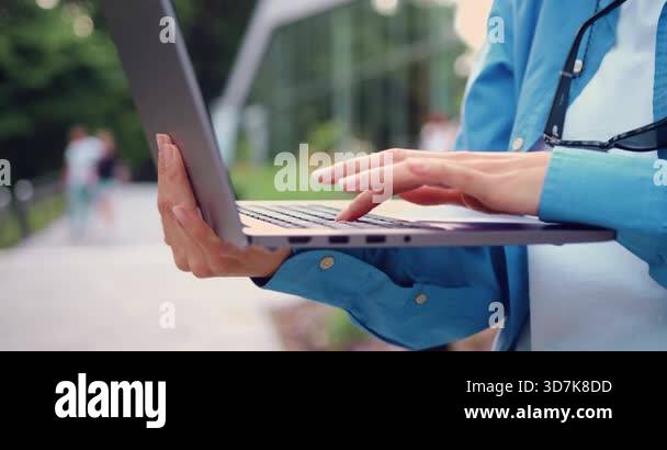 Close-up of female hands typing on a laptop outdoors, working and ...