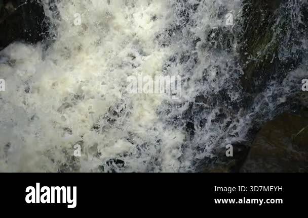 Close-up of foamy white waterfall crashing over dark wet rocks in Ultra ...