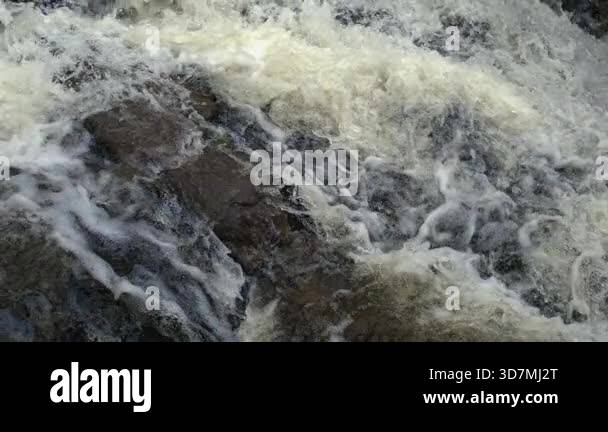 Close-up of turbulent waterfall foam swirling over dark rocks with ...