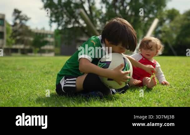 Older brother holding soccer ball while gently pushing younger brother ...