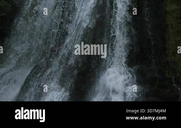 Close-up of waterfall streaming over moss-covered rock face, filmed in ...
