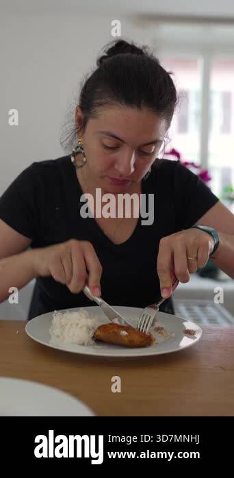 Woman cutting food on plate while sitting at table during meal at home ...