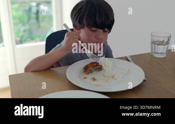 Child leans forward and carefully scoops rice and meat from the plate ...