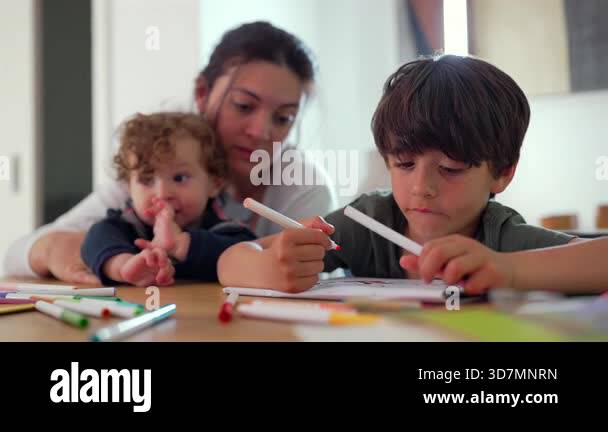 Baby looks toward the boy drawing while mother observes from behind ...