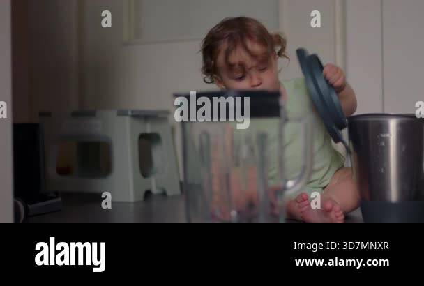Curious toddler sitting on kitchen floor, reaching toward the container ...