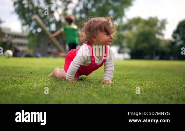 Toddler relaxing on grass facing distant trees, looking into open space ...