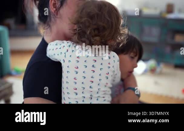 Toddler resting in mother's arms while older child leans in with ...