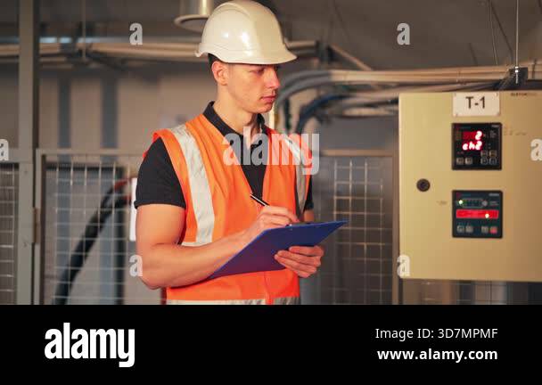 Diligent engineer records crucial data, focusing intently. The industrial setting highlights ...