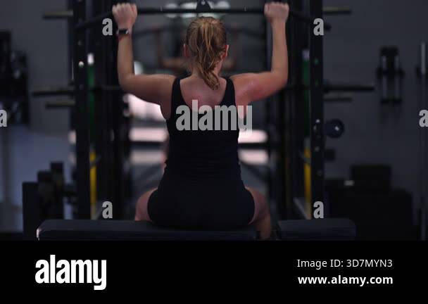 A person exercises at a gym, performing an upper body lift while seated ...
