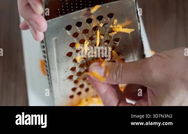 adult fingers grate cheese over container, cheddar cheese is grated by ...