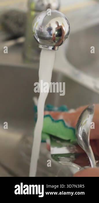 metal spoon being cleaned under tap with green sponge and foamy soap ...
