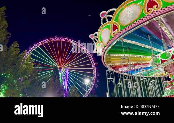 A vibrant amusement park scene at night featuring a colorful carousel ...
