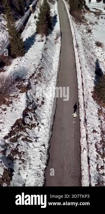 Vertical video aerial drone shot of man athlete runner on the road in ...