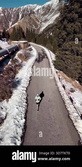 Vertical video aerial drone shot of man athlete runner on the road in ...