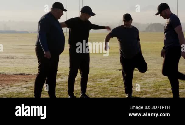 Stepping onto dewy field, senior men linking arms, stretching ...