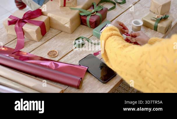 Hand wearing yellow sweater reaching for red ribbon and wrapping green ...