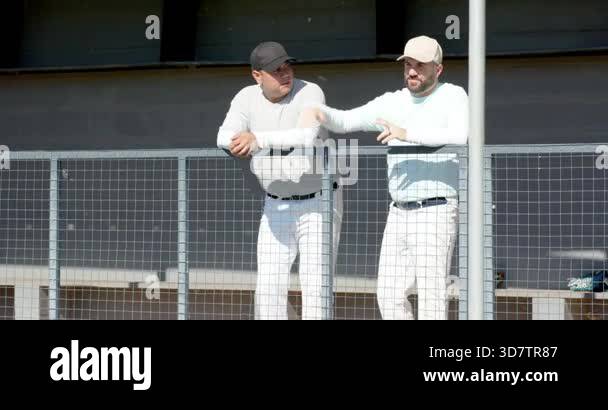 High-fiving catcher, two male baseball players leaning on fence ...