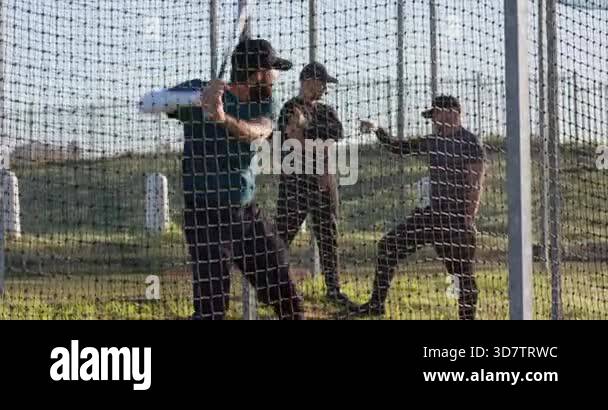Coach throwing pitch, male batter swinging white bat in cage practicing ...