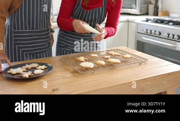 Seeing uniced cookies on rack, Diverse couple piping white icing in ...