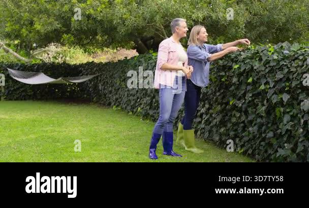 Female friends trimming ivy hedge in garden pointing at growth and ...